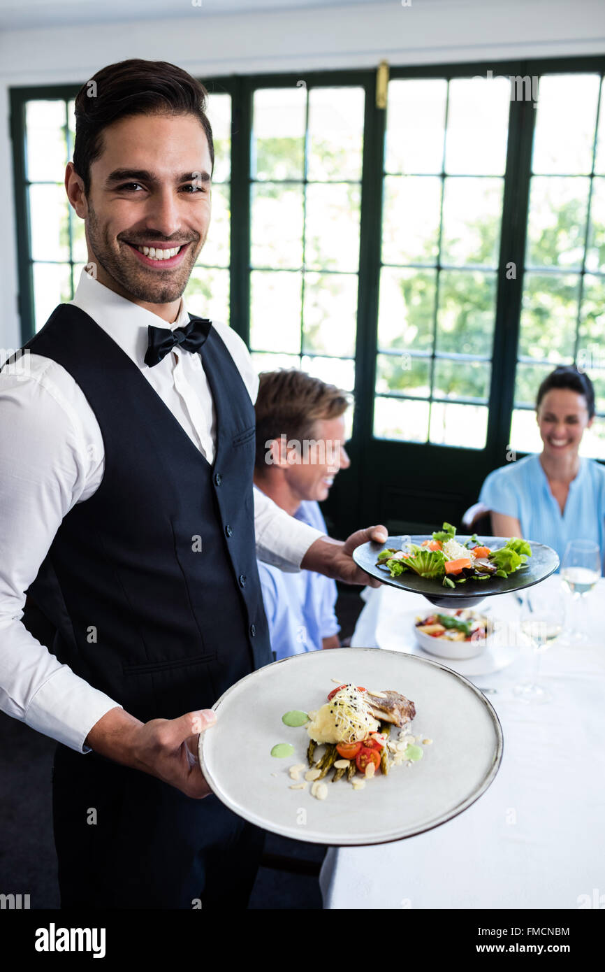 Portrait of waiter standing with meal next to customers Stock Photo - Alamy