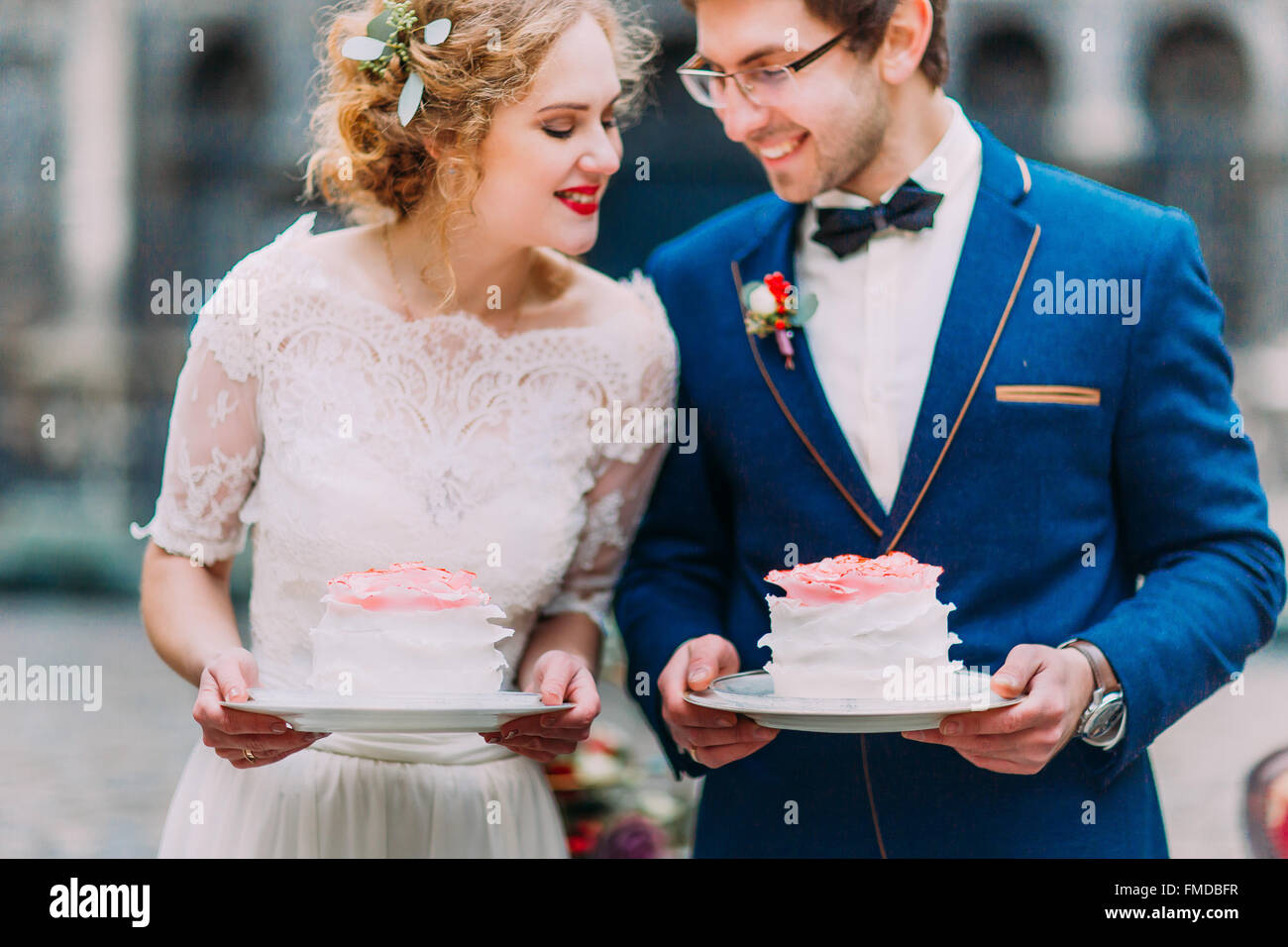 Charming newlyweds holding pieces of their wedding cakes and happily ...