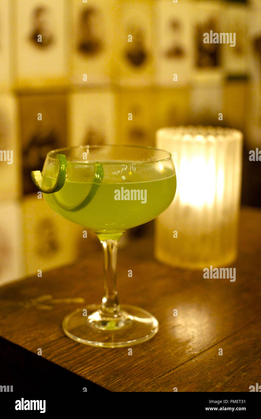 A green cocktail sits on a wooden bar top with a candle burning in the ...
