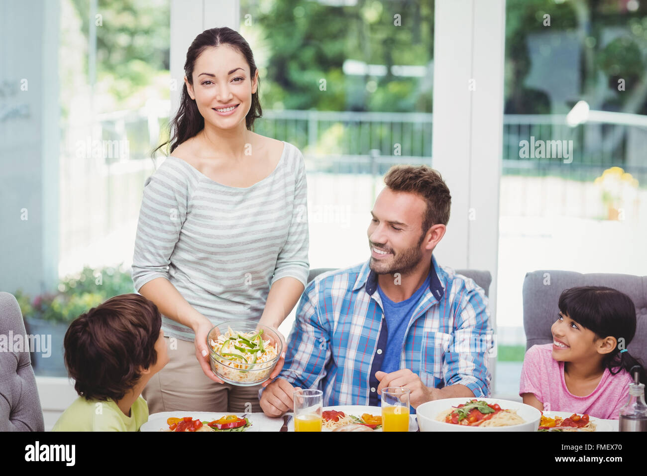 Smiling mother standing at dining table with family Stock Photo - Alamy