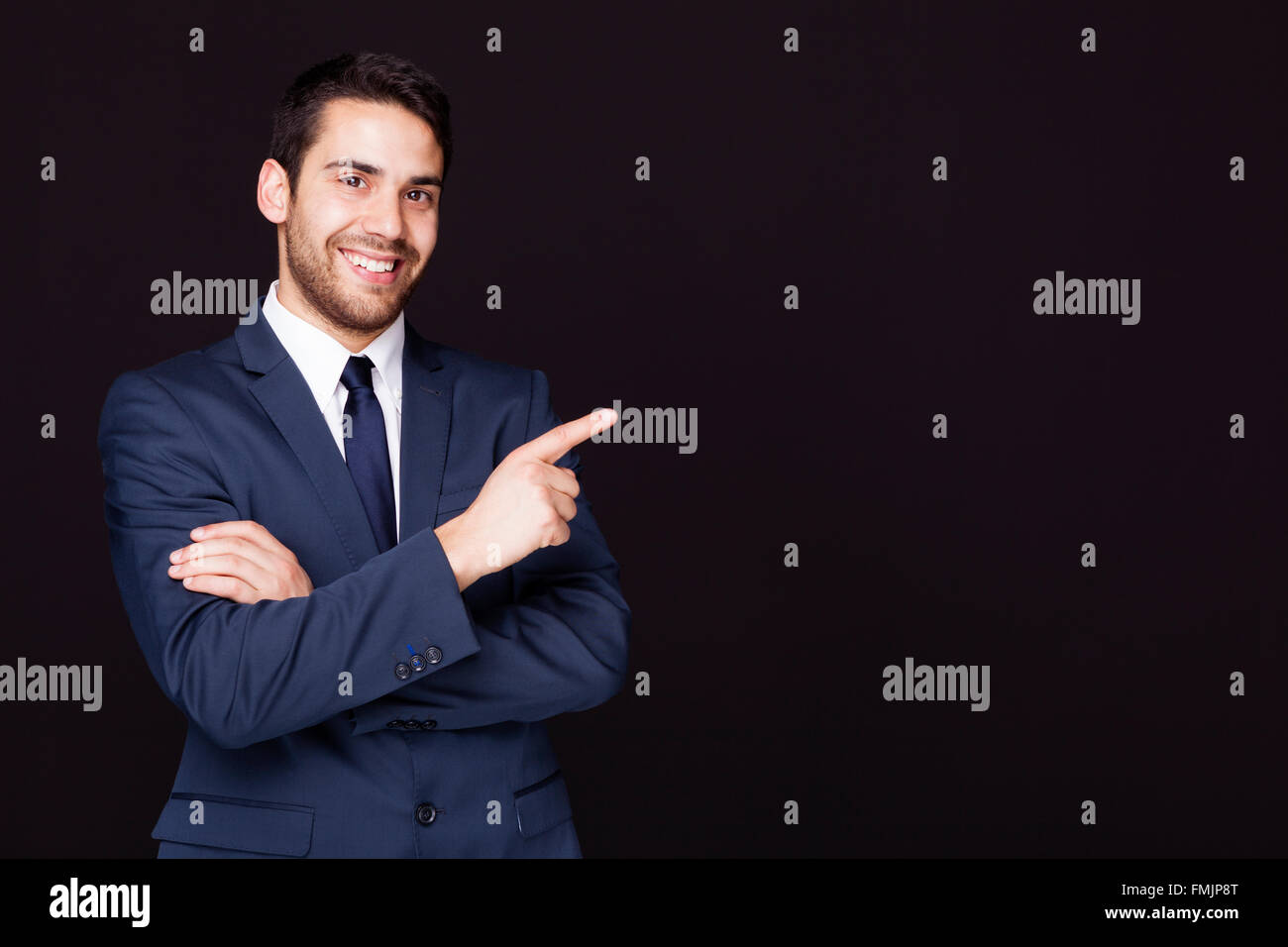 Handsome business man pointing at something against dark background ...
