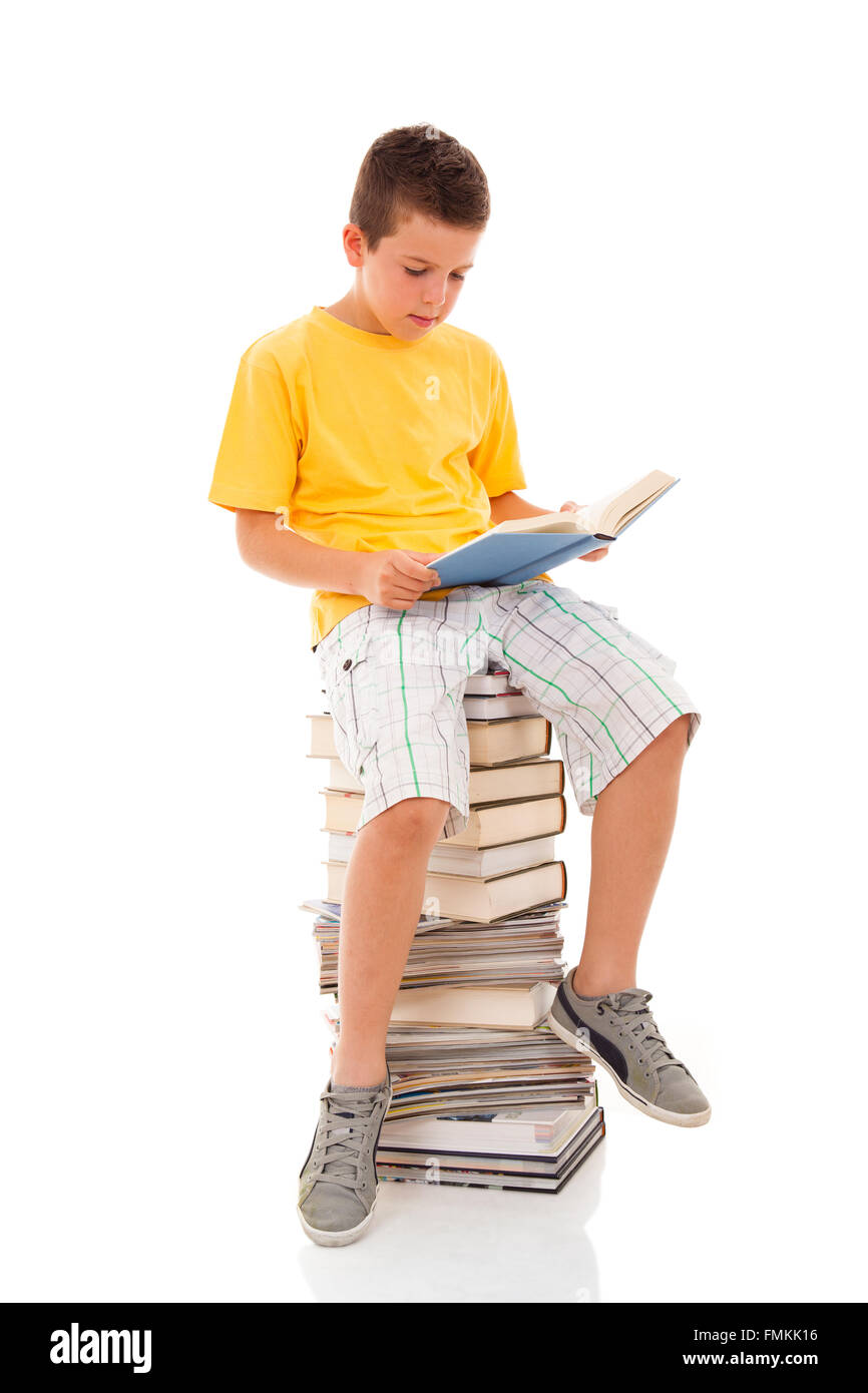 Young boy sitting on a pile of books reading against a white background ...