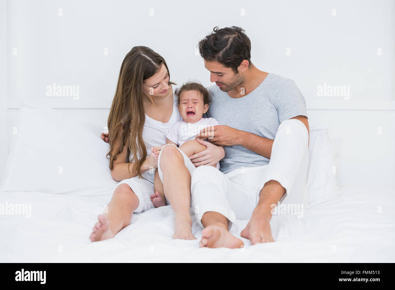Parents with crying baby sitting on bed Stock Photo - Alamy
