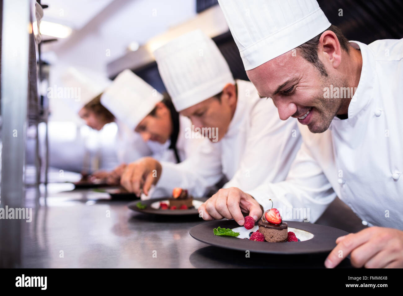 Team of chefs finishing dessert plates in the kitchen Stock Photo - Alamy