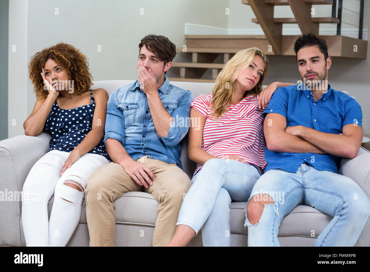 Upset young friends on sofa in living room Stock Photo - Alamy