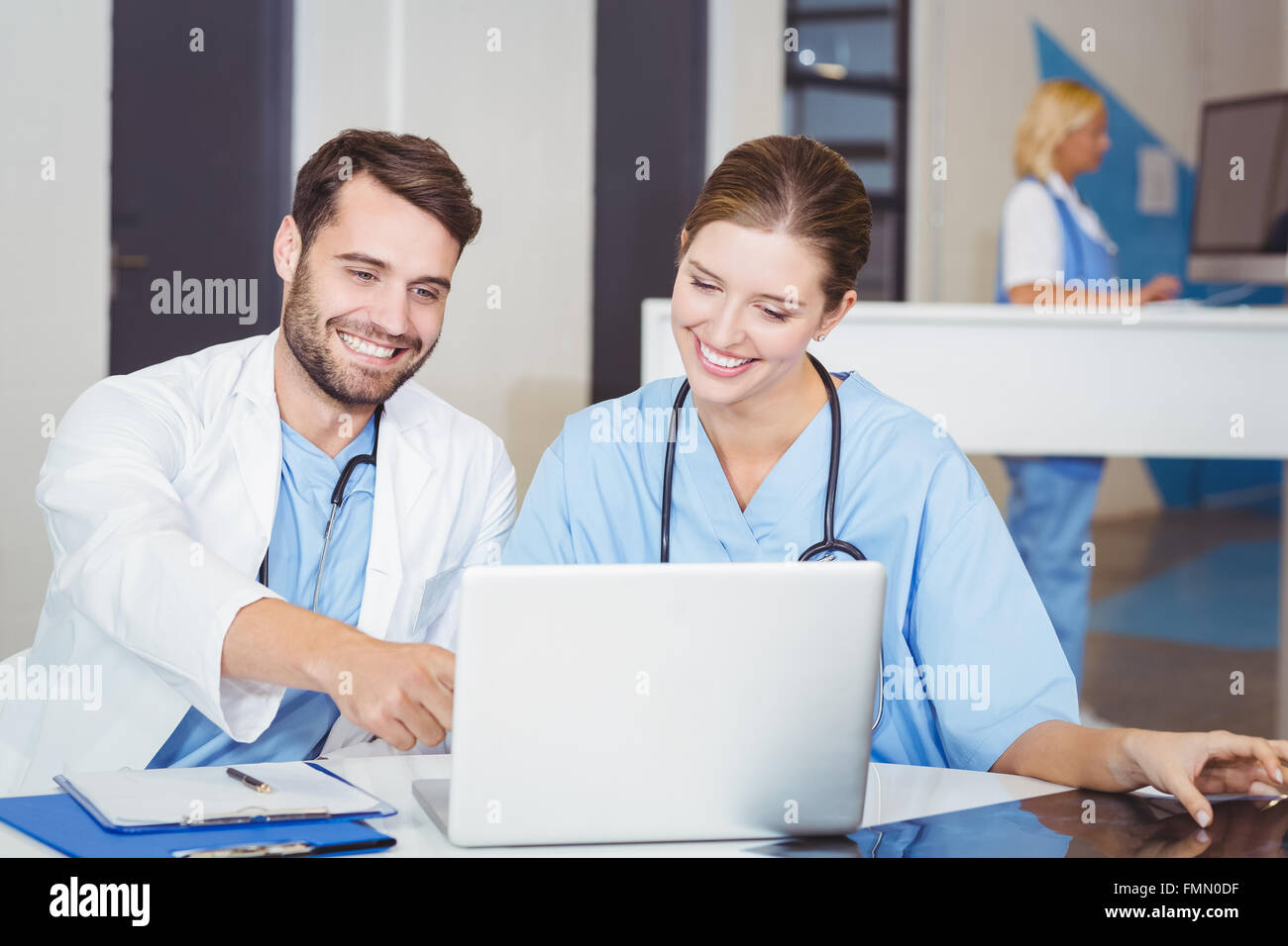Happy doctors using laptop while discussing at desk Stock Photo - Alamy