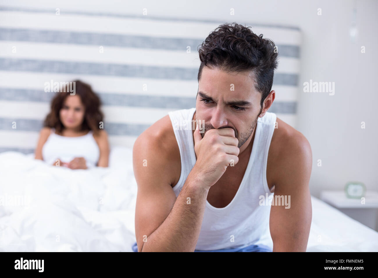 Tensed man sitting on bed while wife in background Stock Photo - Alamy