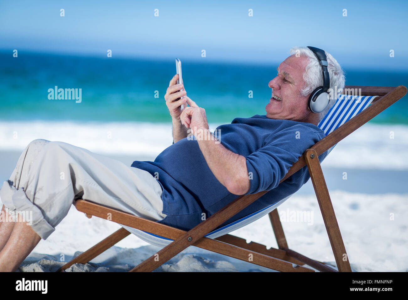Mature man resting on a deck chair listening to music with smartphone ...