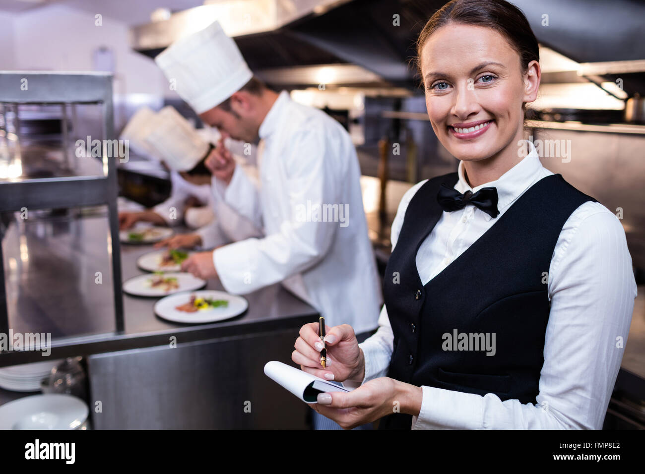Smiling waitress with note pad in commercial kitchen Stock Photo - Alamy