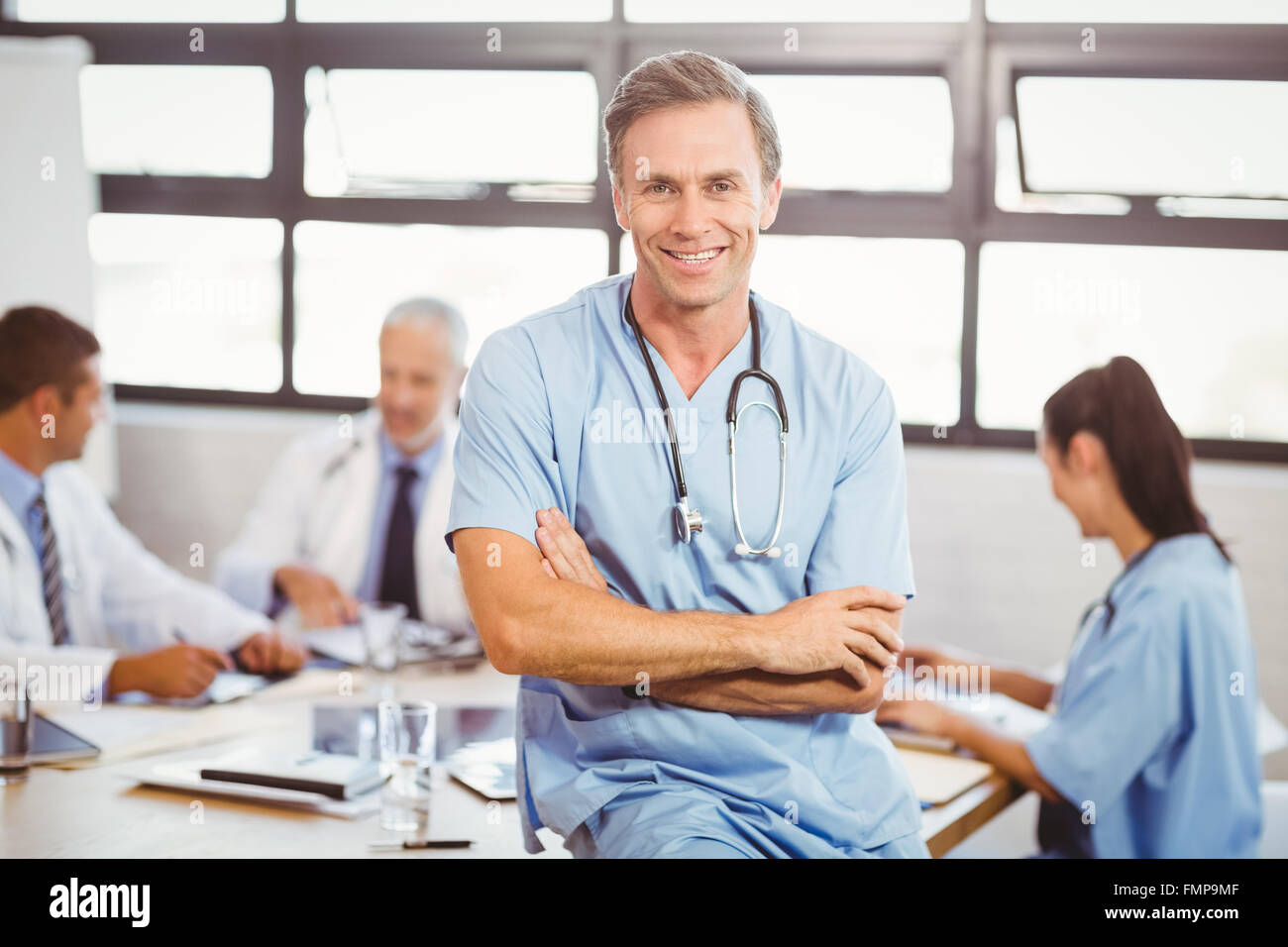 Portrait of male doctor sitting on table with arms crossed Stock Photo ...