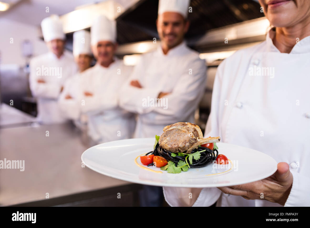 Team of chefs with one presenting a dish Stock Photo - Alamy