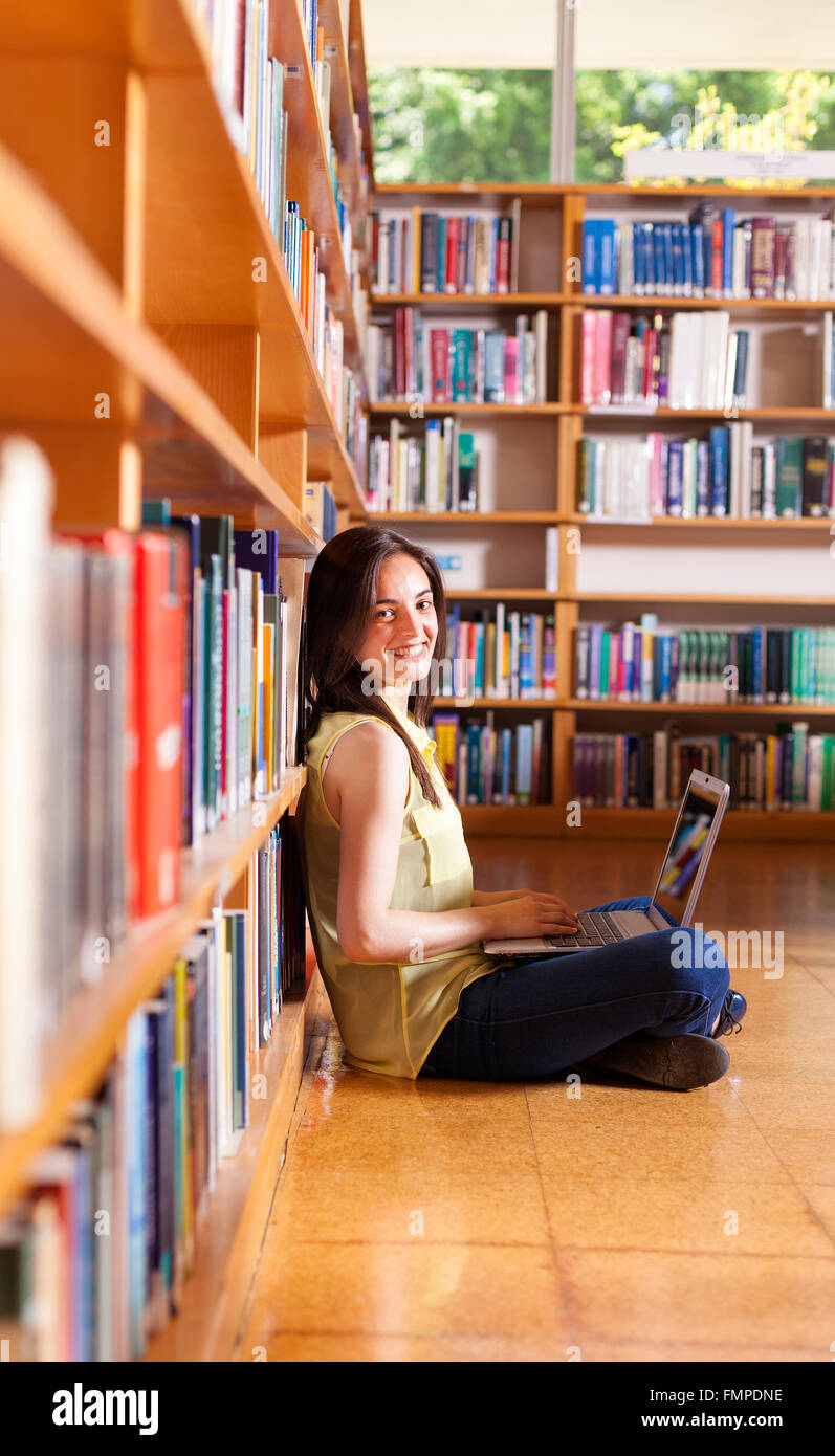 Young smiling student using her laptop in a library Stock Photo - Alamy