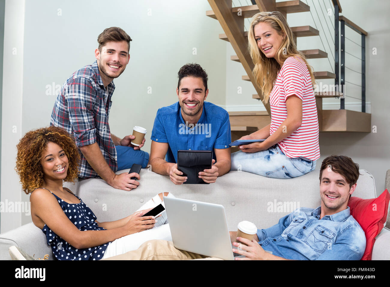 Happy young friends using modern technologies on sofa Stock Photo - Alamy