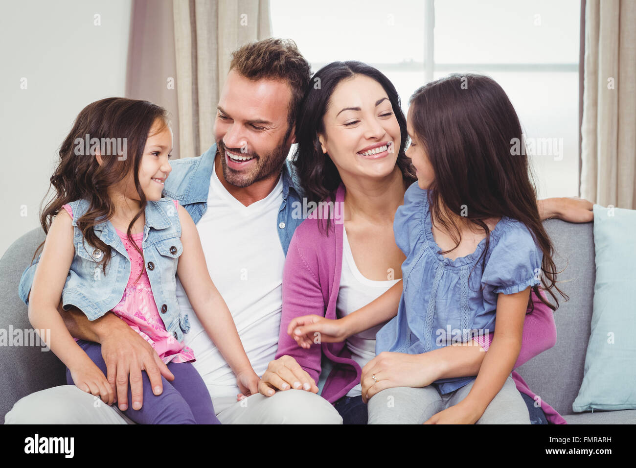 Parents smiling while sitting with daughters on sofa Stock Photo - Alamy