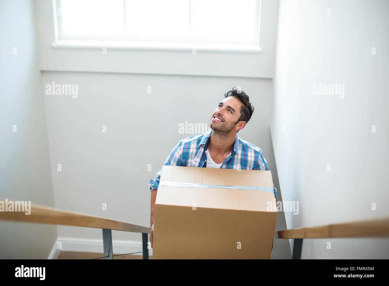 Smiling man holding cardboard box while climbing steps Stock Photo - Alamy