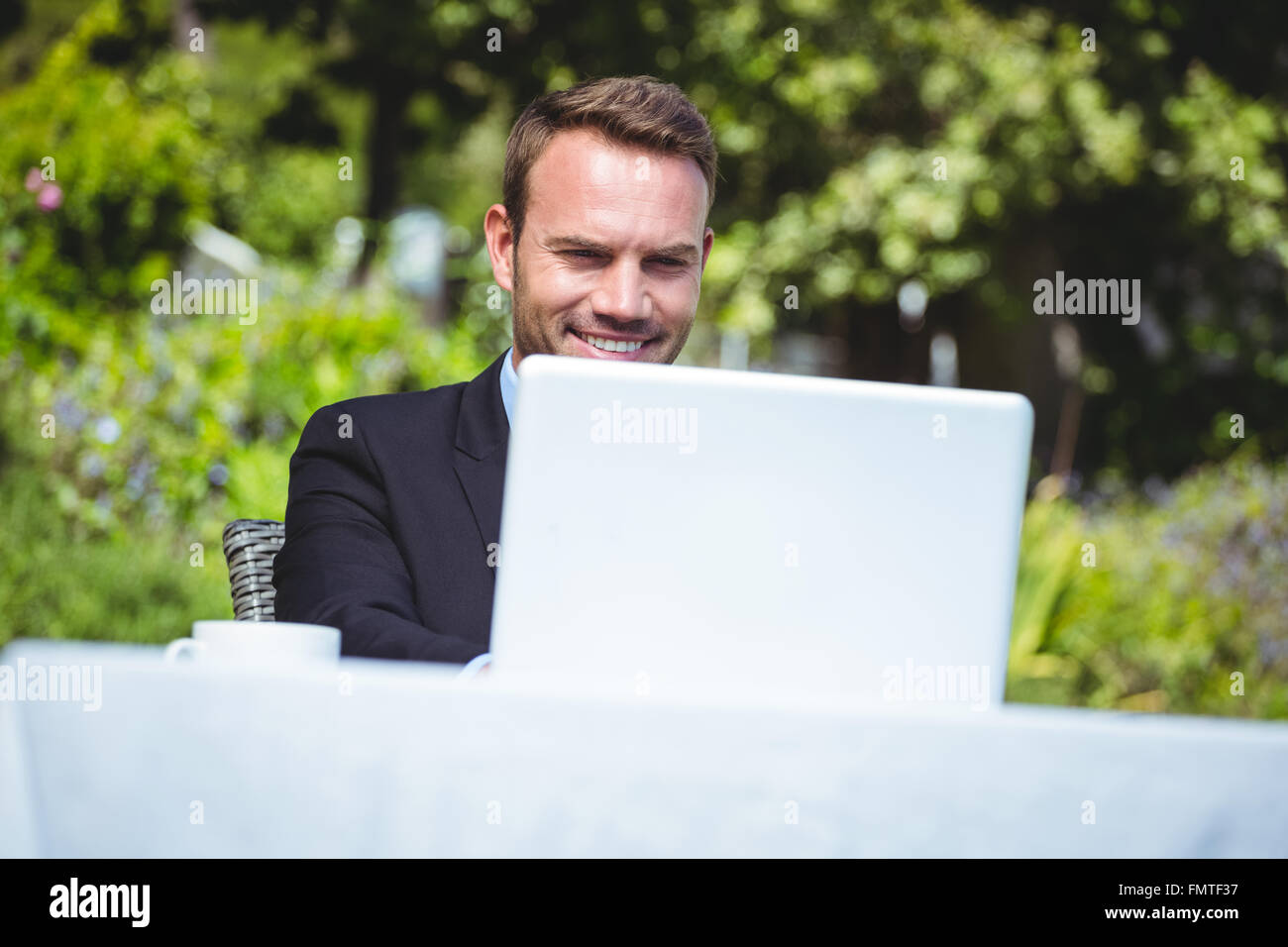 Smiling businessman using laptop and having a coffee Stock Photo - Alamy