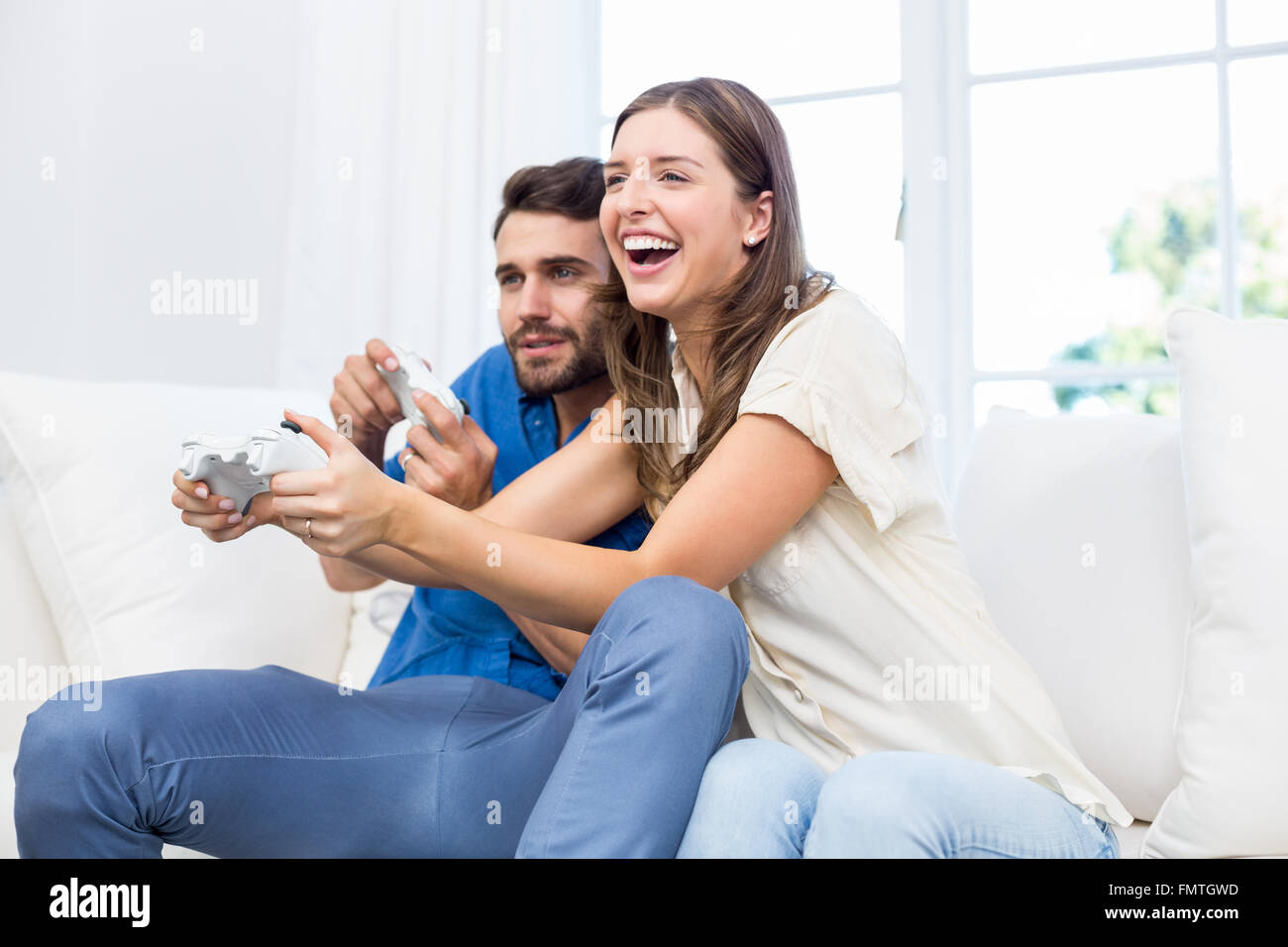 Couple playing video game while sitting on sofa Stock Photo - Alamy