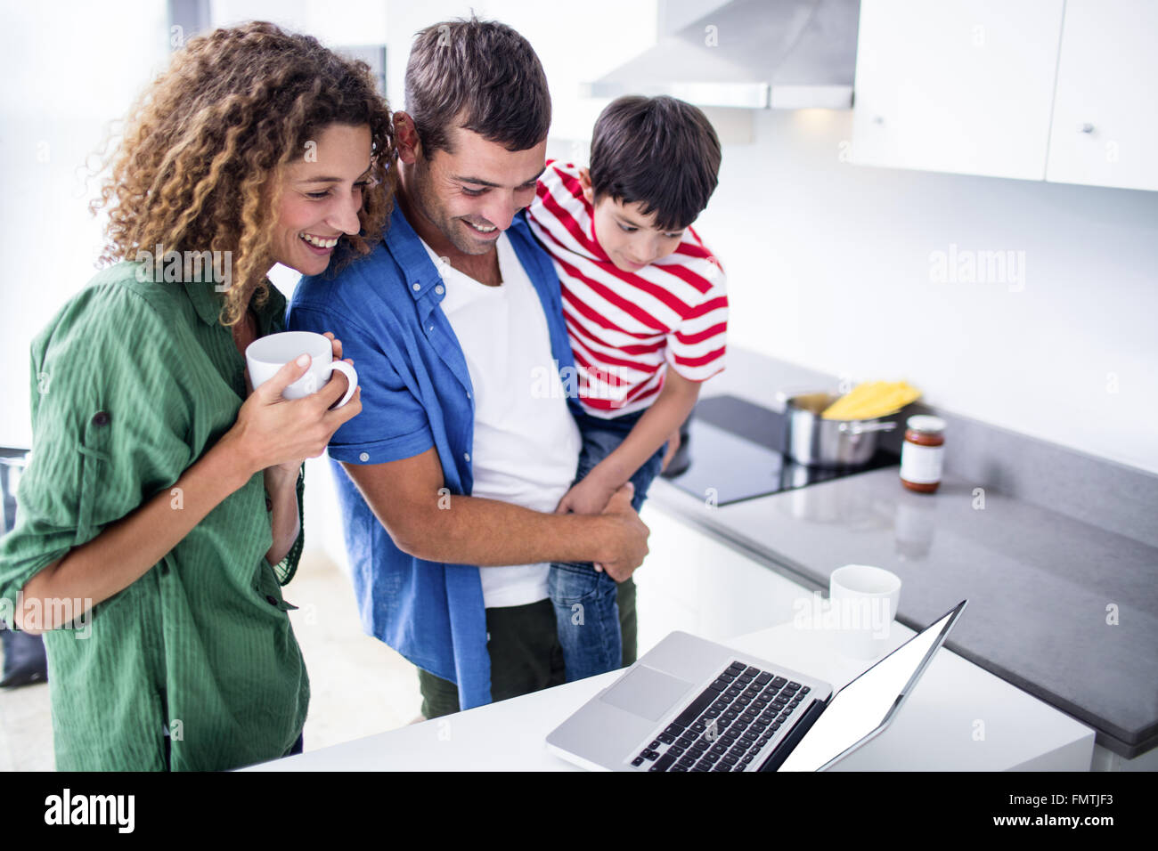 Parents using laptop with son in kitchen Stock Photo - Alamy