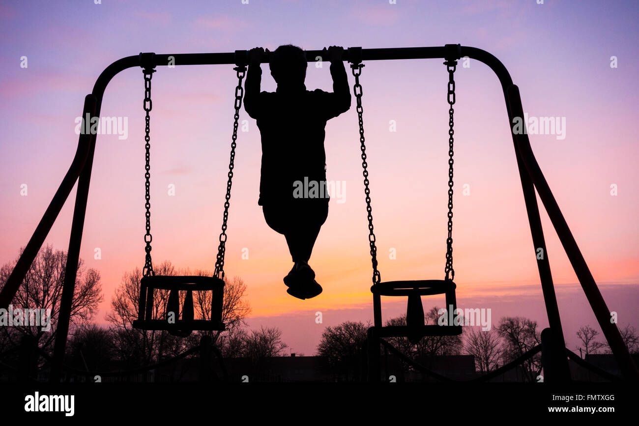Man doing pull ups on swing frame at sunrise in public park in England ...