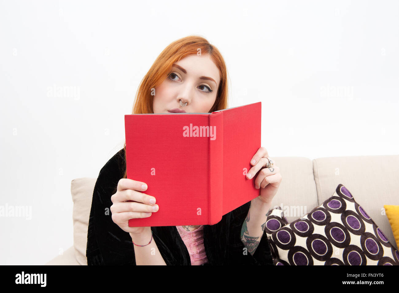 Young redhead woman reading a book with red cover looking out left ...