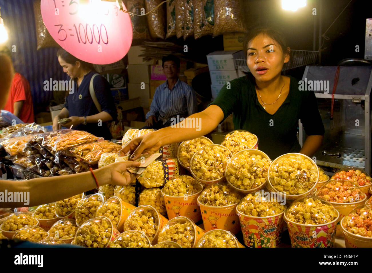 A woman is selling popcorn from Thailand to a customer at a street fair ...