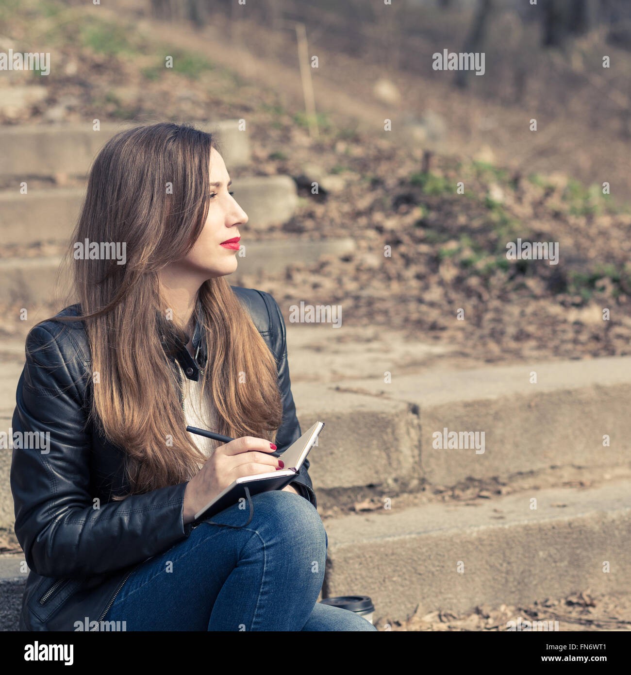 Young woman sitting on stairs in the park writing in a pad. Adult ...