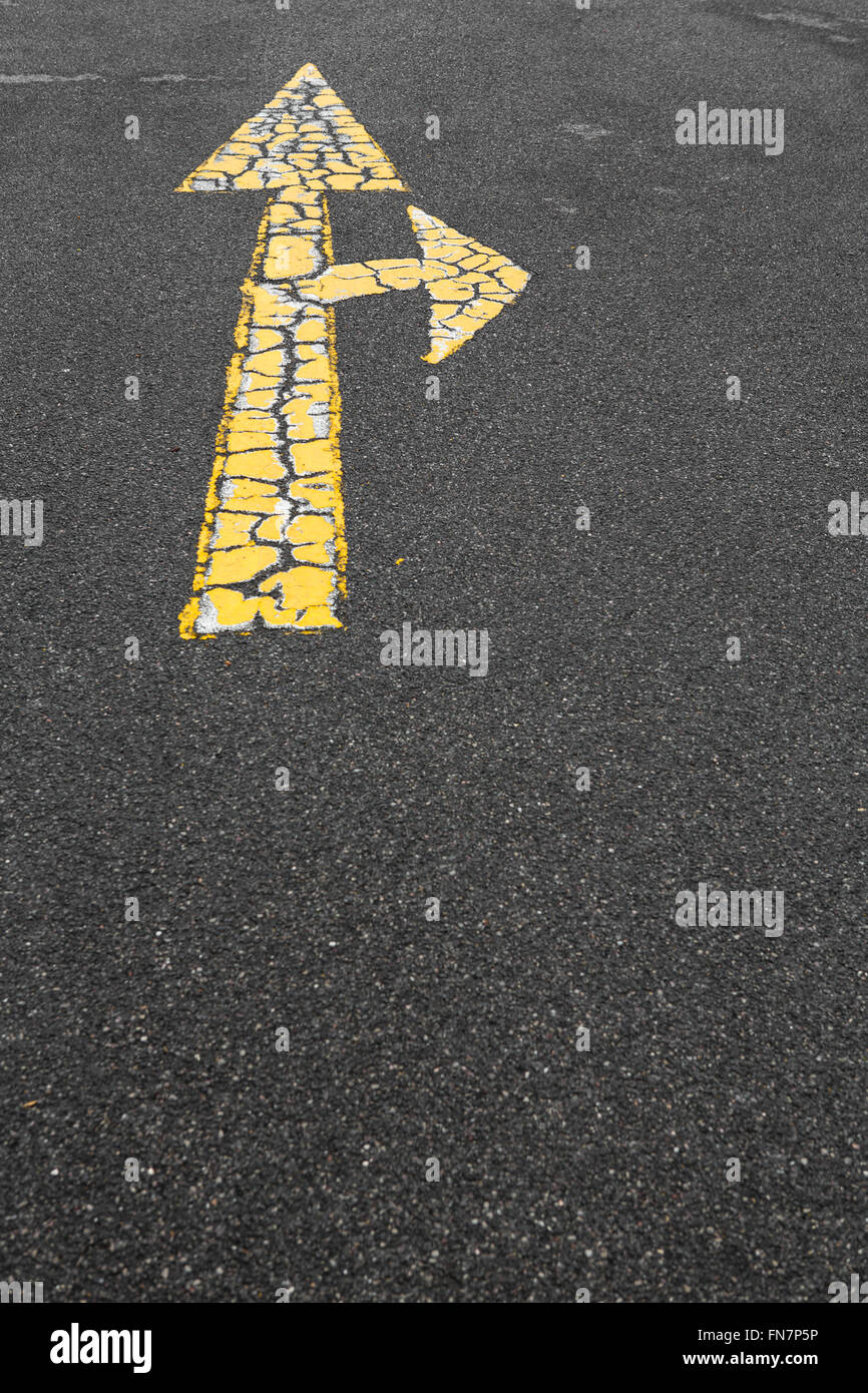 An old painted and faded arrow sign on the tarmac of a road indicating ...