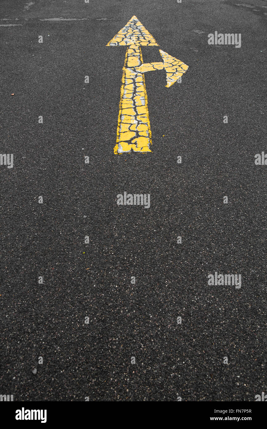 An old painted and faded arrow sign on the tarmac of a road indicating ...