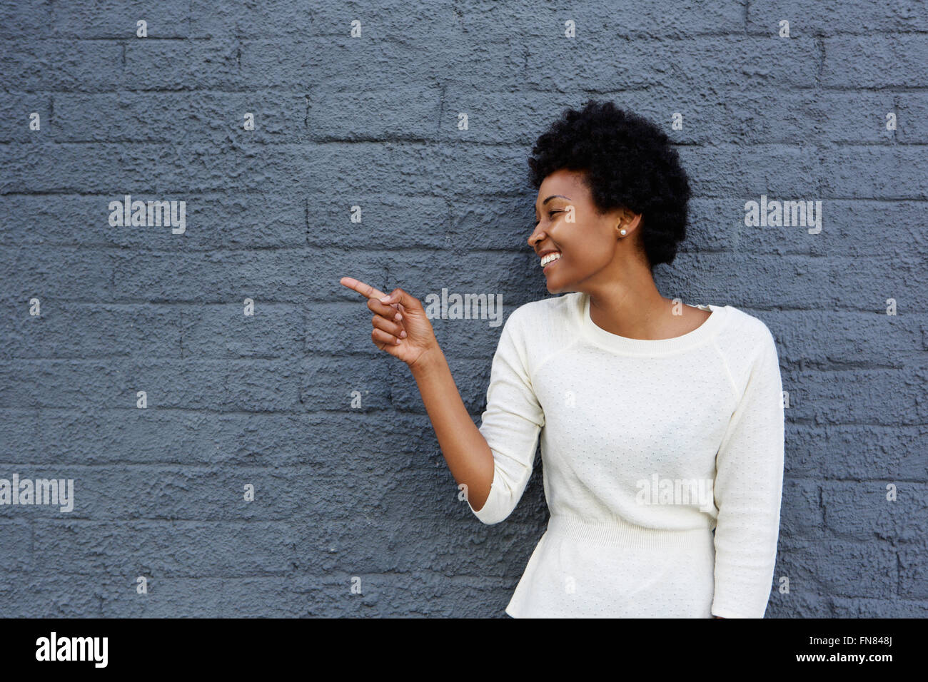 Portrait of happy young african woman pointing at copy space on gray ...