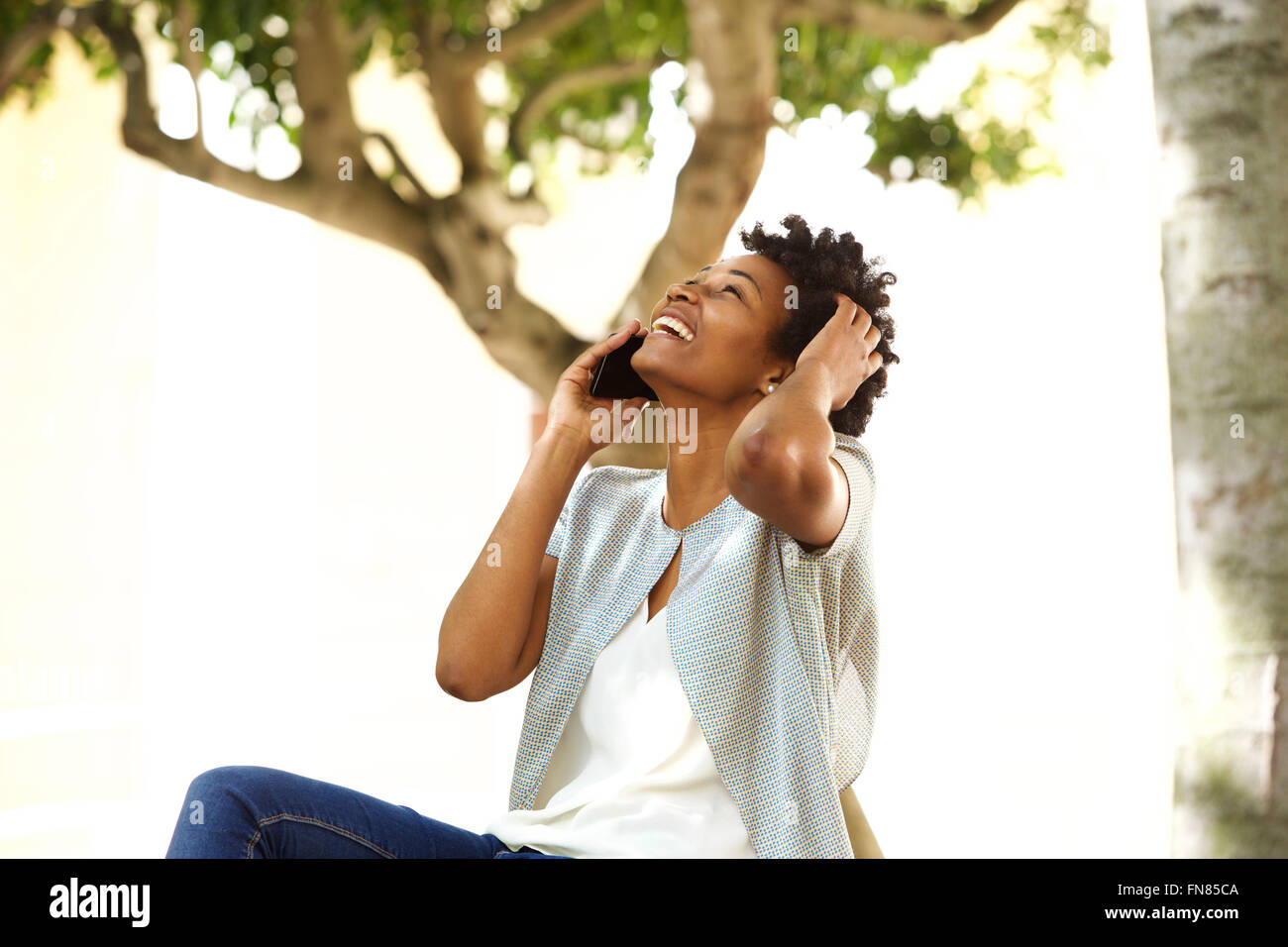 Portrait of cheerful young woman sitting outside talking on mobile ...