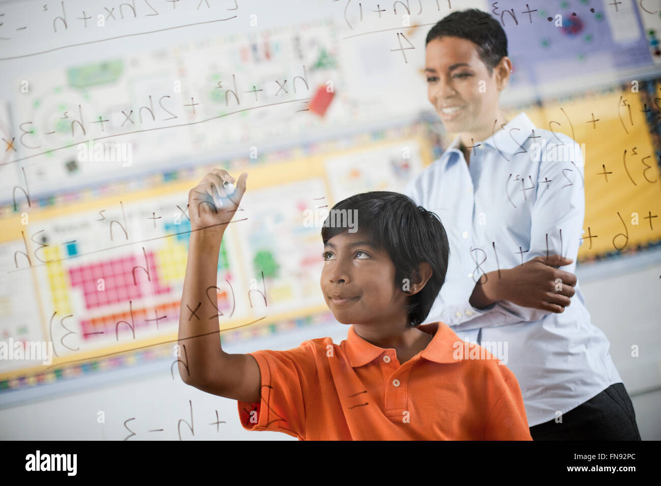 A student writing formula and equations on a clear perspex board, with ...