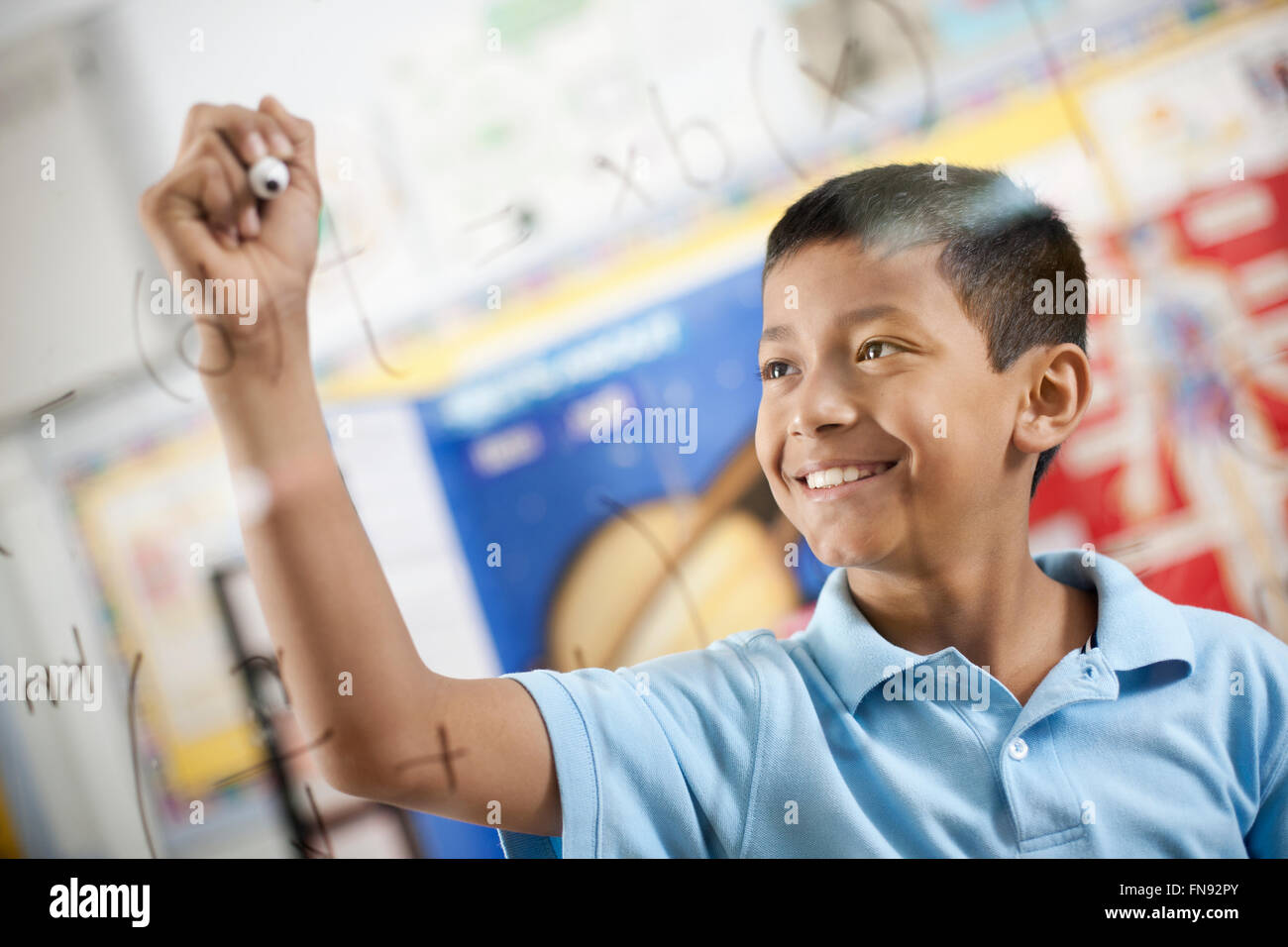 A boy writing scientific equations on a clear perspex board with a felt ...
