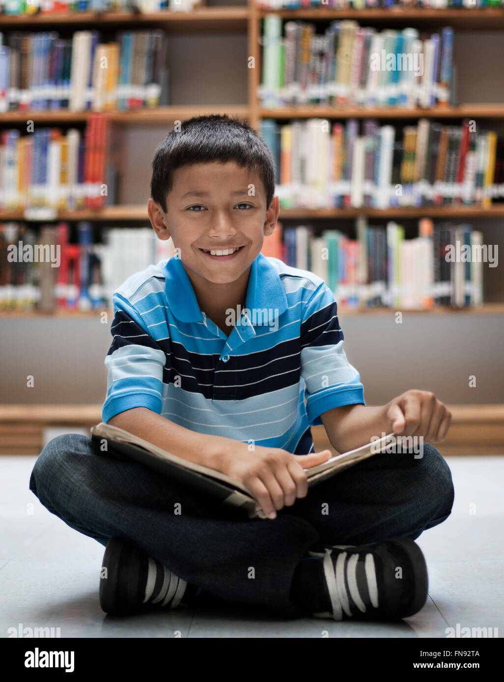 A boy sitting on the floor in a library reading a book Stock Photo - Alamy
