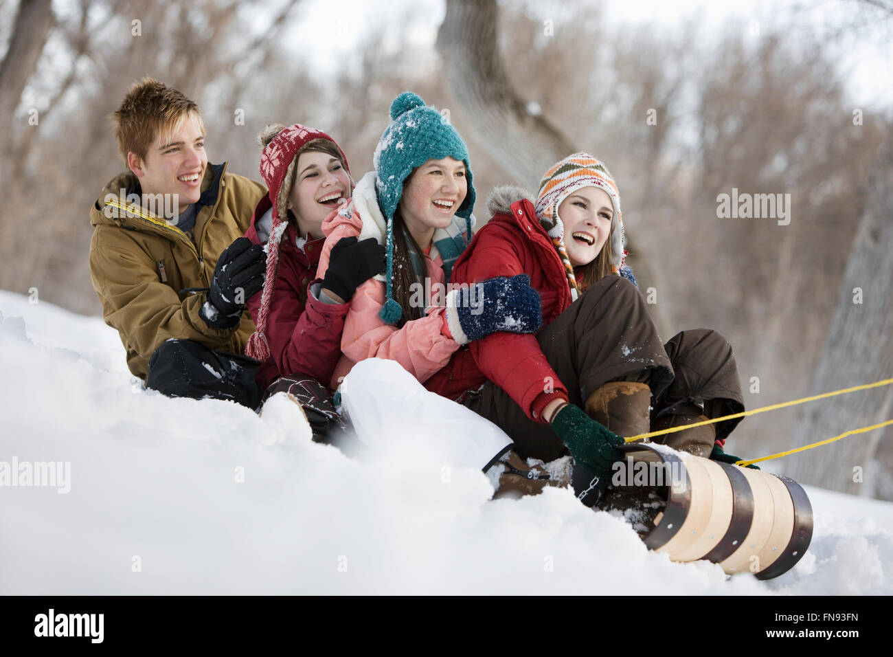 Four young people on a large sledge sliding across the snow, downhill ...