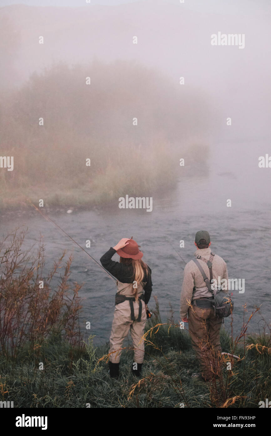 Two people, man and woman standing on the riverbank looking across the ...
