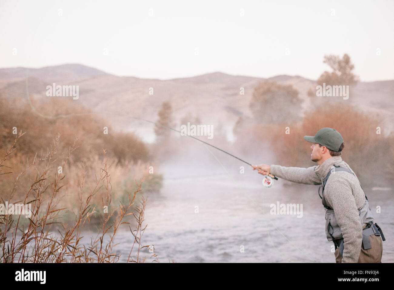 A man standing casting his fishing rod, fly fishing from a riverbank ...