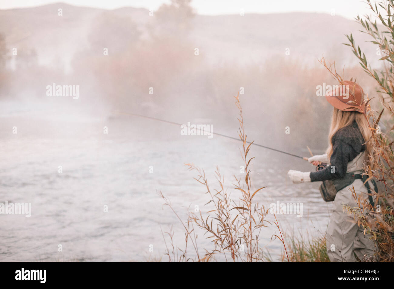 A fisherman, a woman standing on the banks of a river, fly fishing ...
