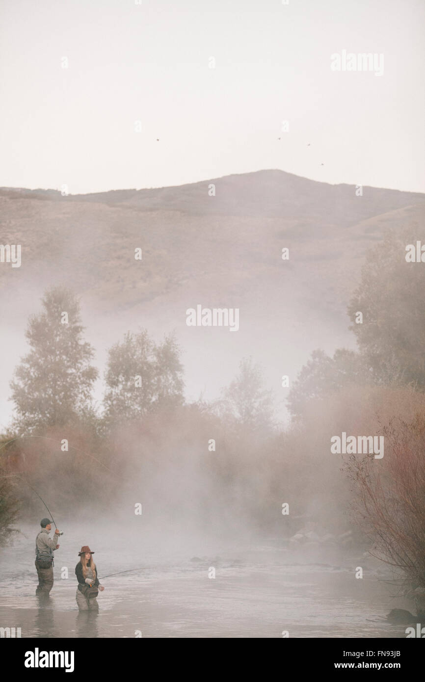 A couple, a man and woman standing in mid stream fly fishing in a river ...