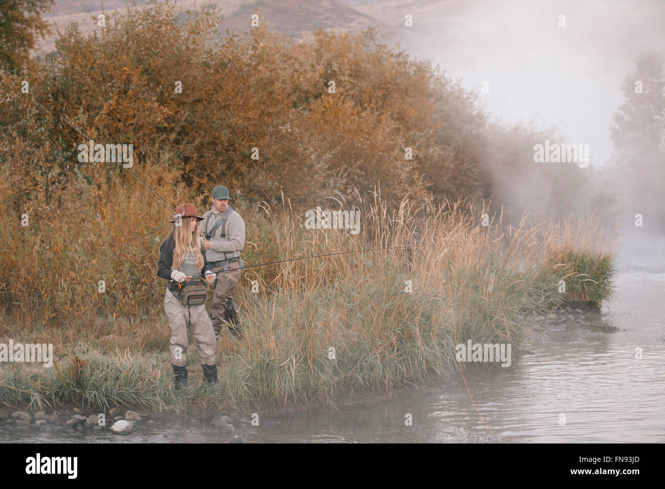 A man and woman standing on a riverbank, fishing Stock Photo - Alamy