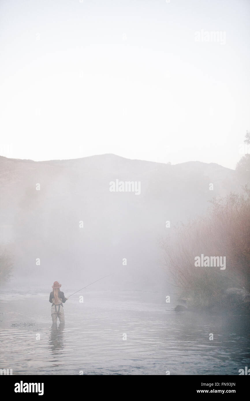 A woman fisherman fly fishing, standing in waders in thigh deep water ...