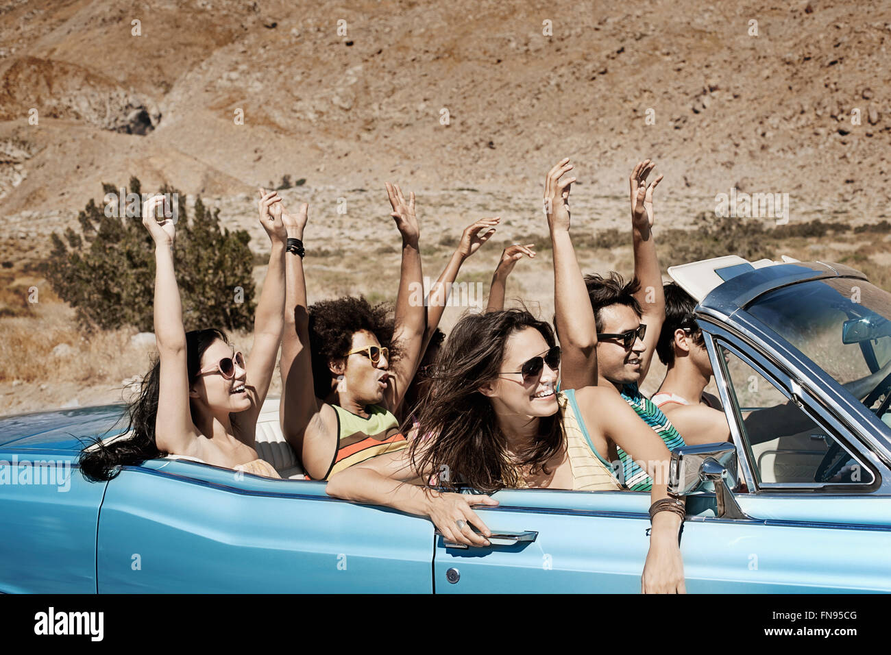 A group of friends in a pale blue convertible on the open road, driving ...