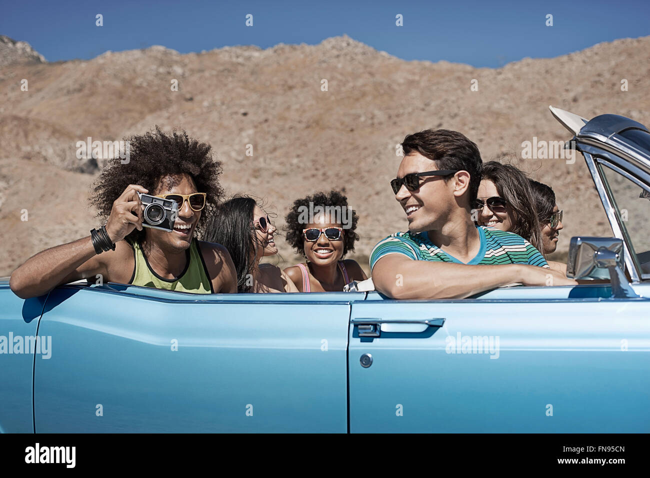 A group of friends in a pale blue convertible on the open road, driving ...
