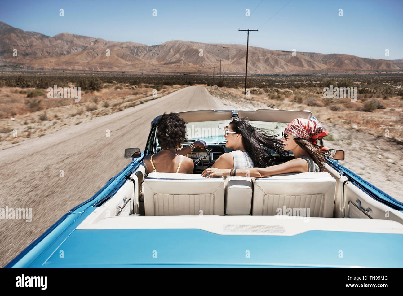 Three young people in a pale blue convertible car, driving on the open ...