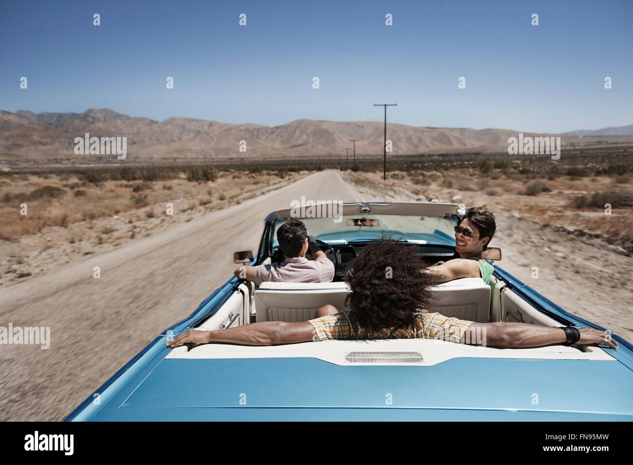 Three young people in a pale blue convertible car, driving on the open ...