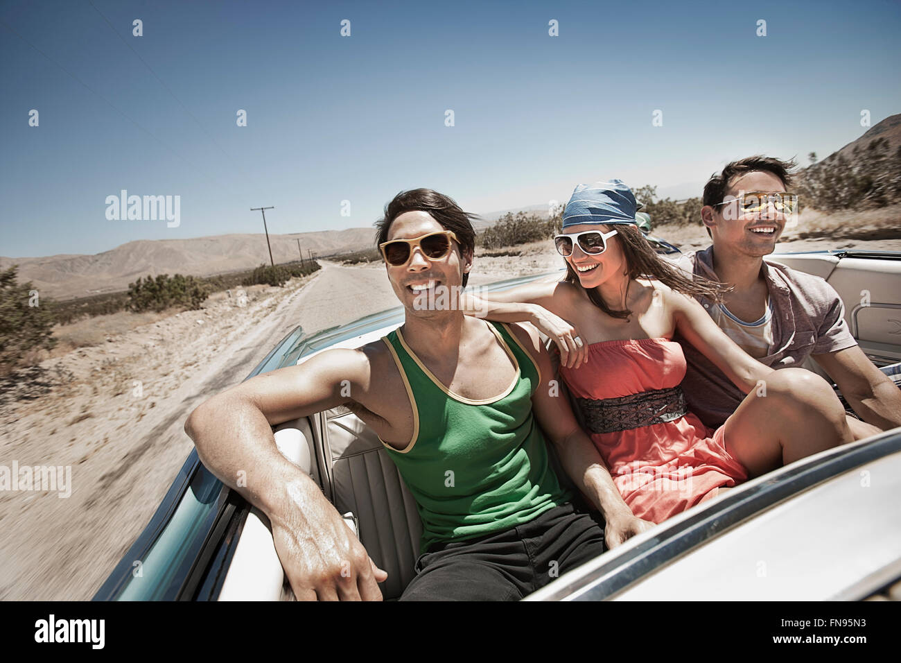 Three young people in a pale blue convertible car, driving on the open ...