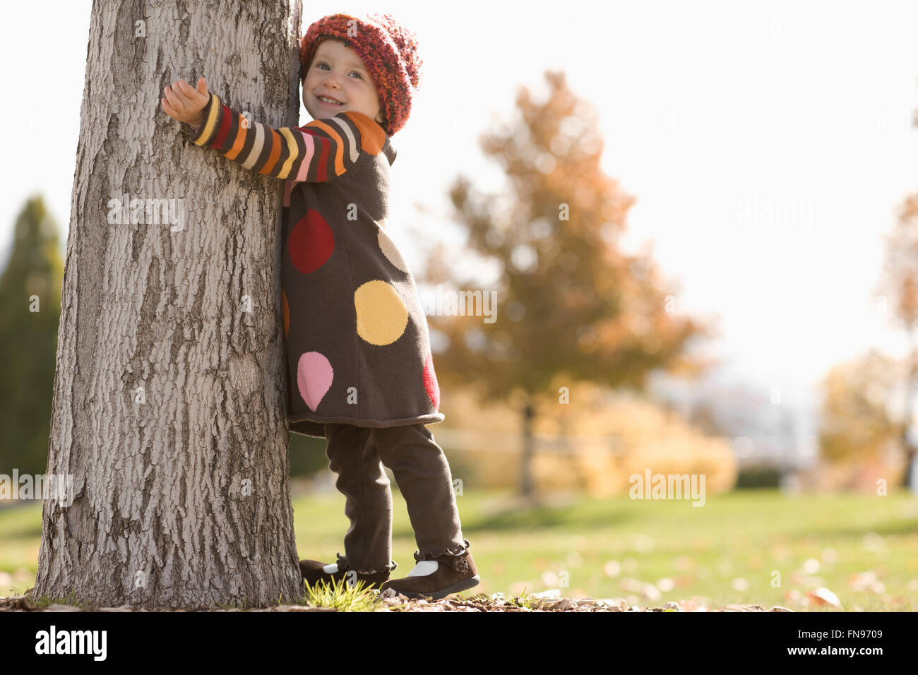 A young girl with her arms around a tree in autumn sunshine Stock Photo ...