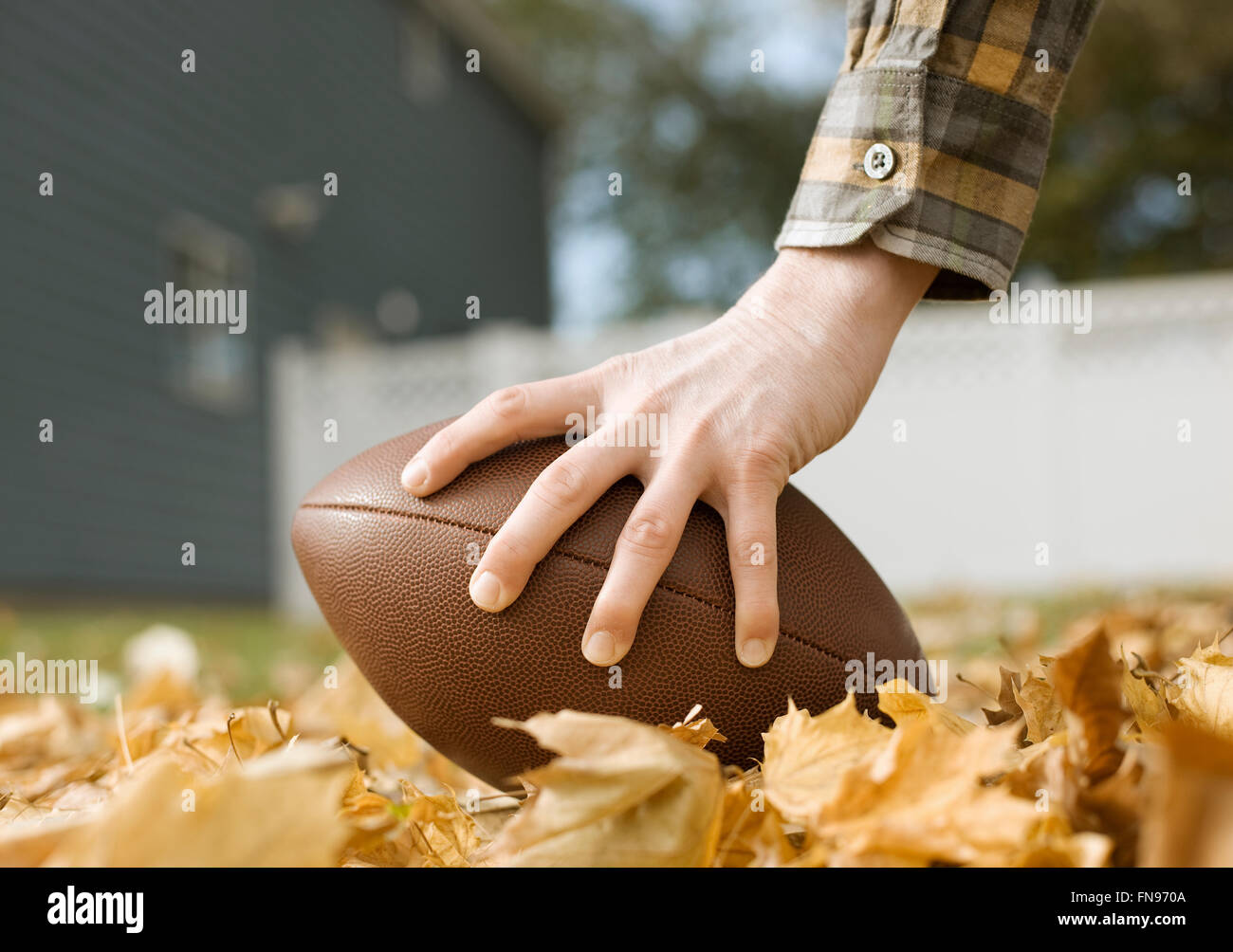 A person's hand holding an oval football on the ground, among fallen ...