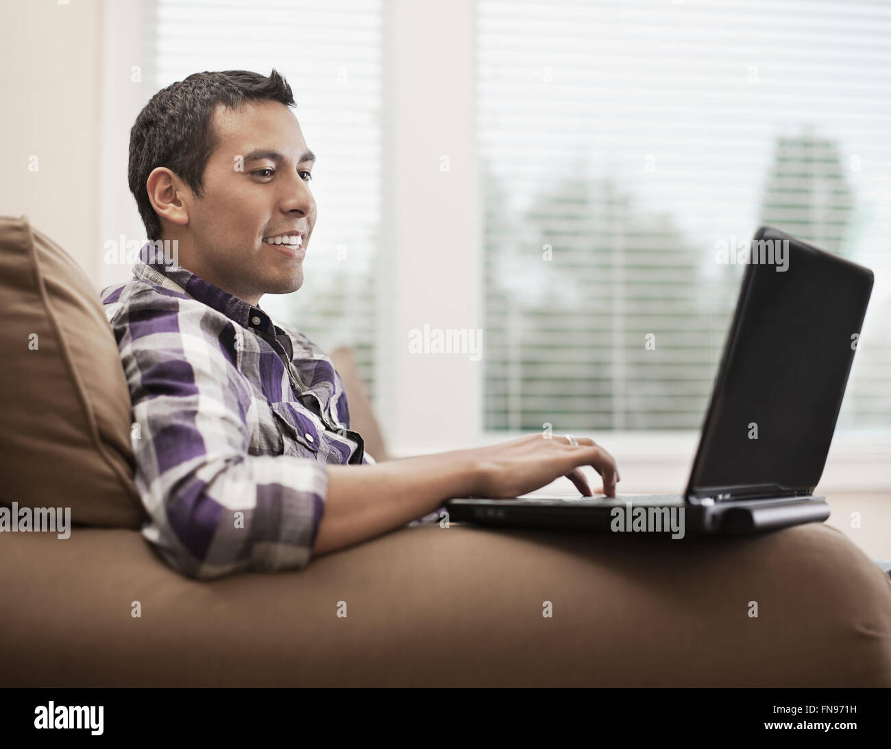 A man seated on a sofa, using a laptop computer Stock Photo - Alamy