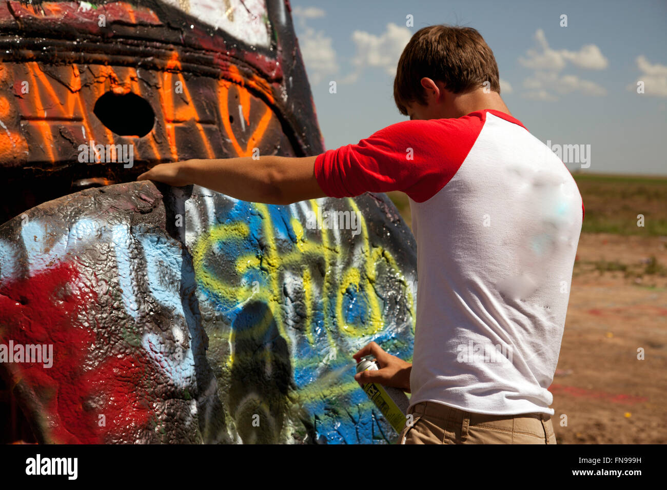A teenage boy spray painting a car at Cadillac Ranch in Amarillo, Texas ...