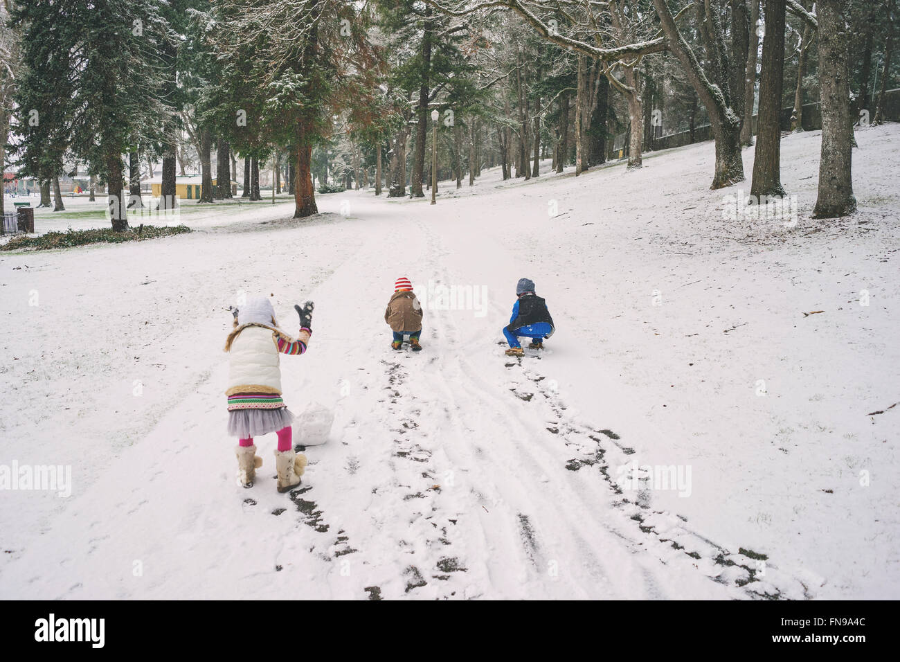Two boys and girl rolling snowballs down hill in a park Stock Photo - Alamy